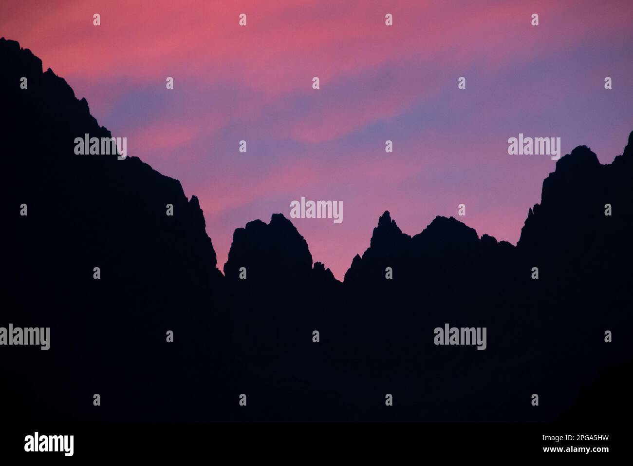 Rugged peaks of the mountain range are silhouetted against a stunning ...