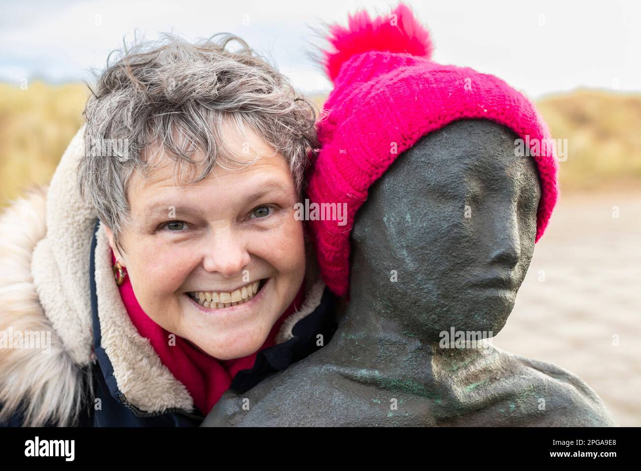 middle aged woman smiling with metal sculpture of person with pink ...