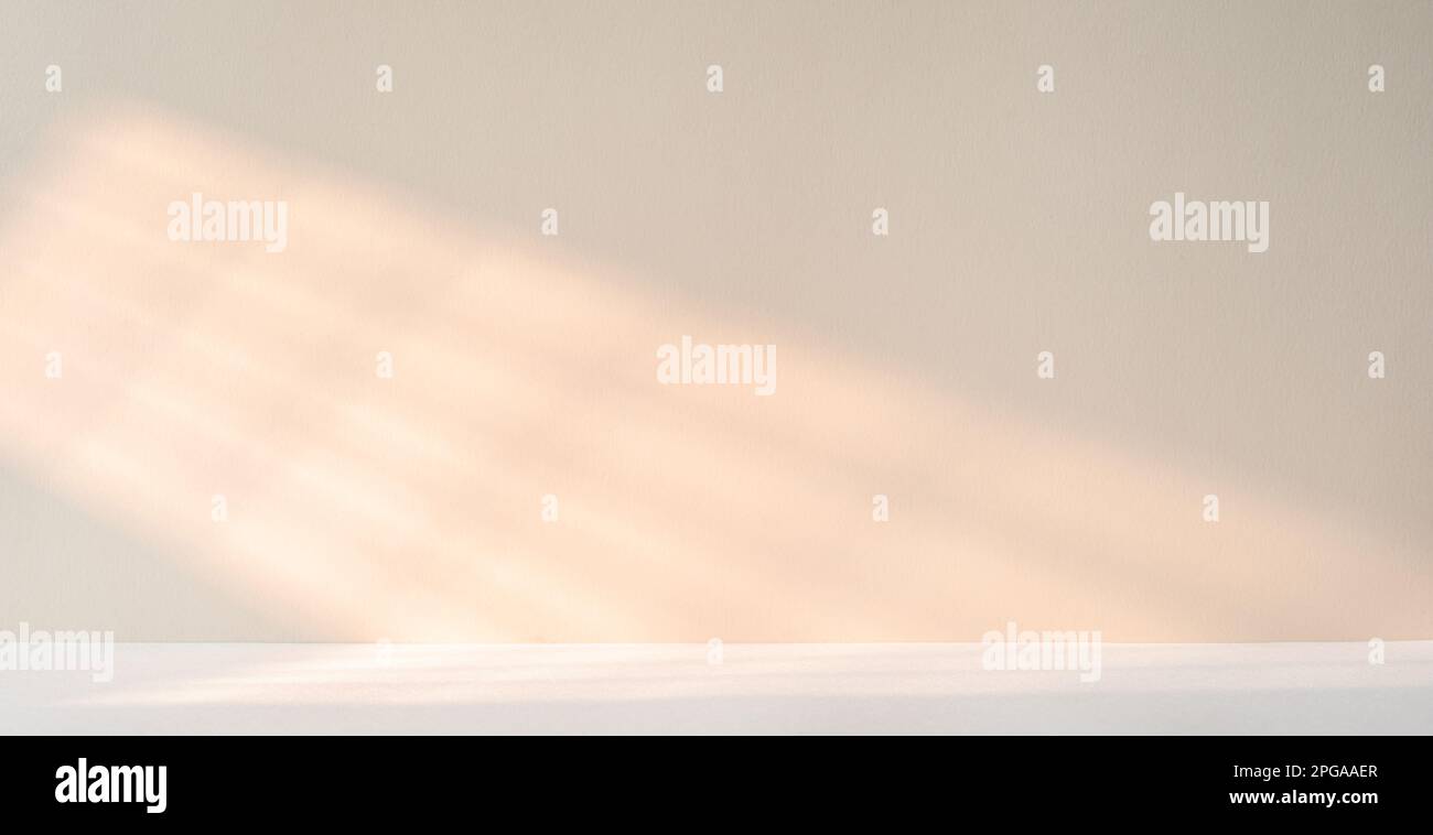 A light beige wall with sunlight beams and white table or floor for ...