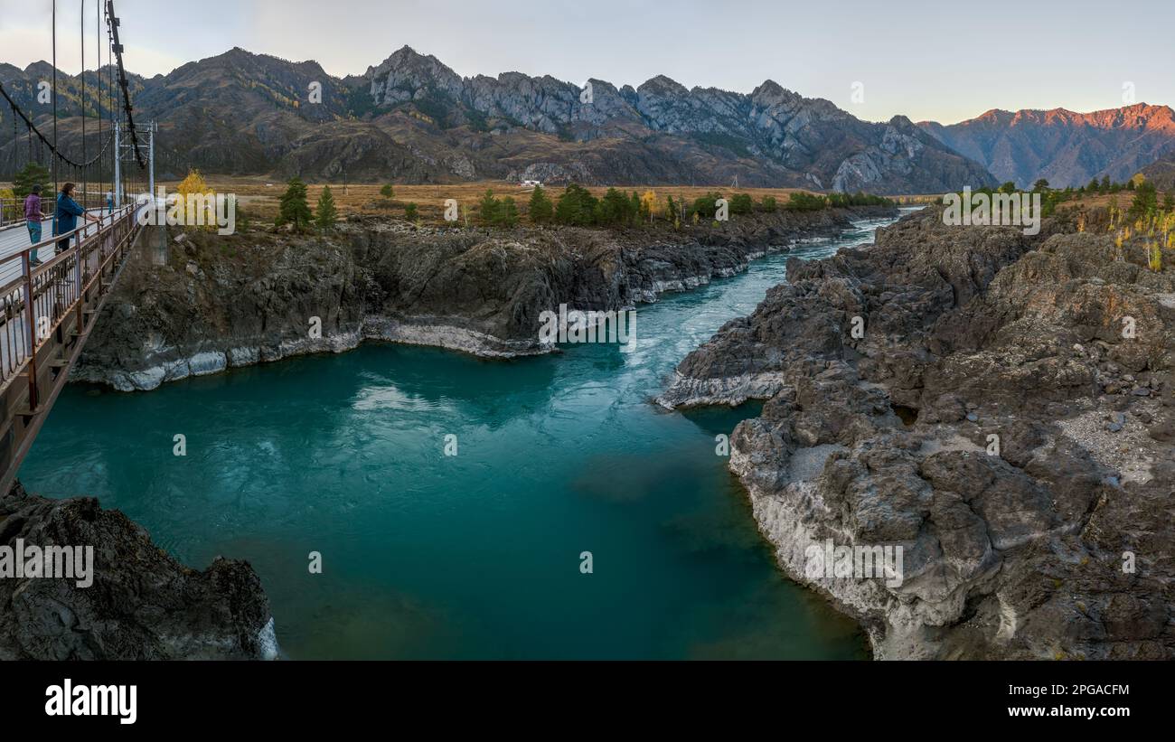 Two women hikers walk on a bridge across the mountain river Katun with ...