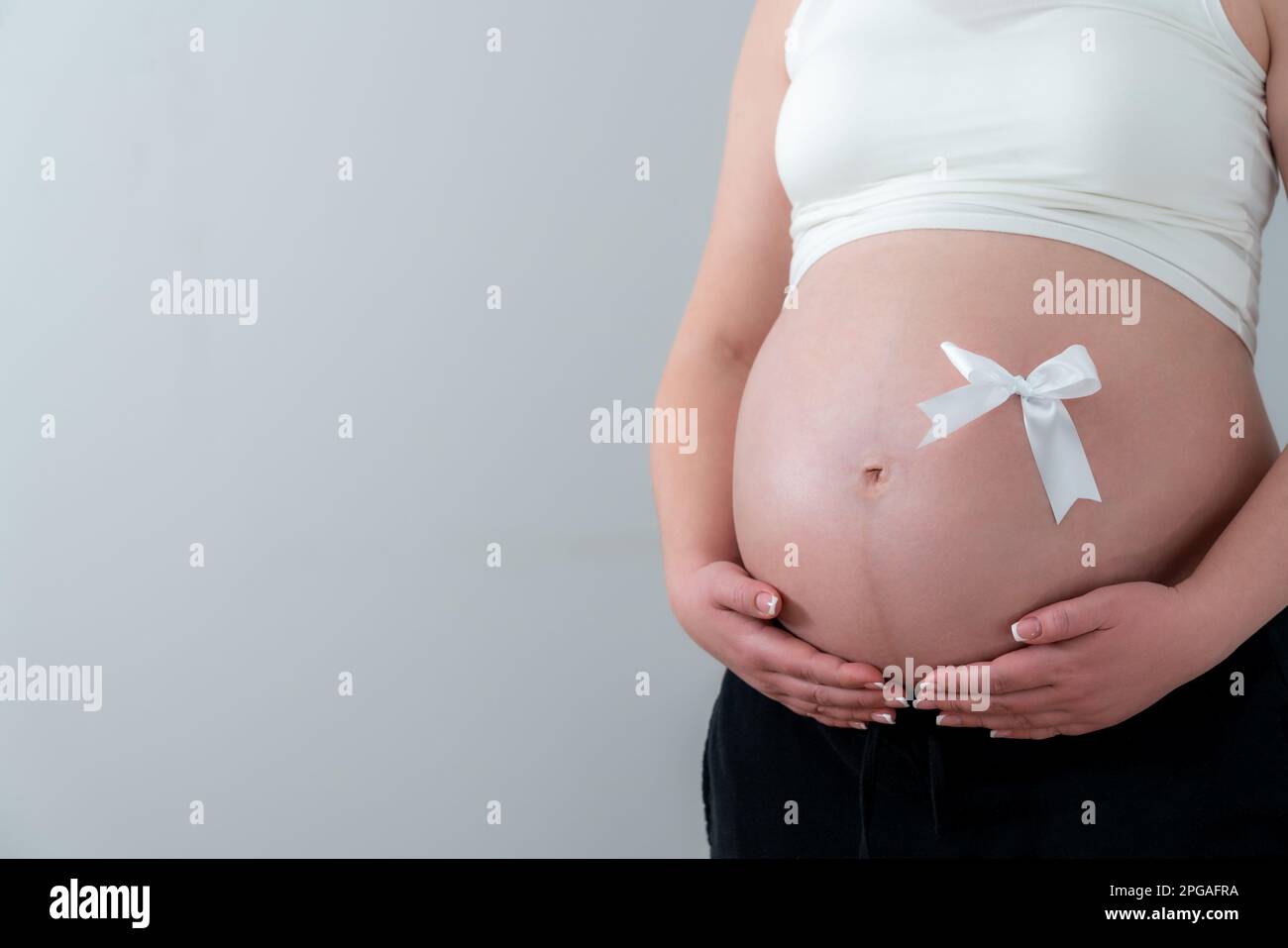 Beautiful female belly in late pregnancy with a white bow as a gift to ...
