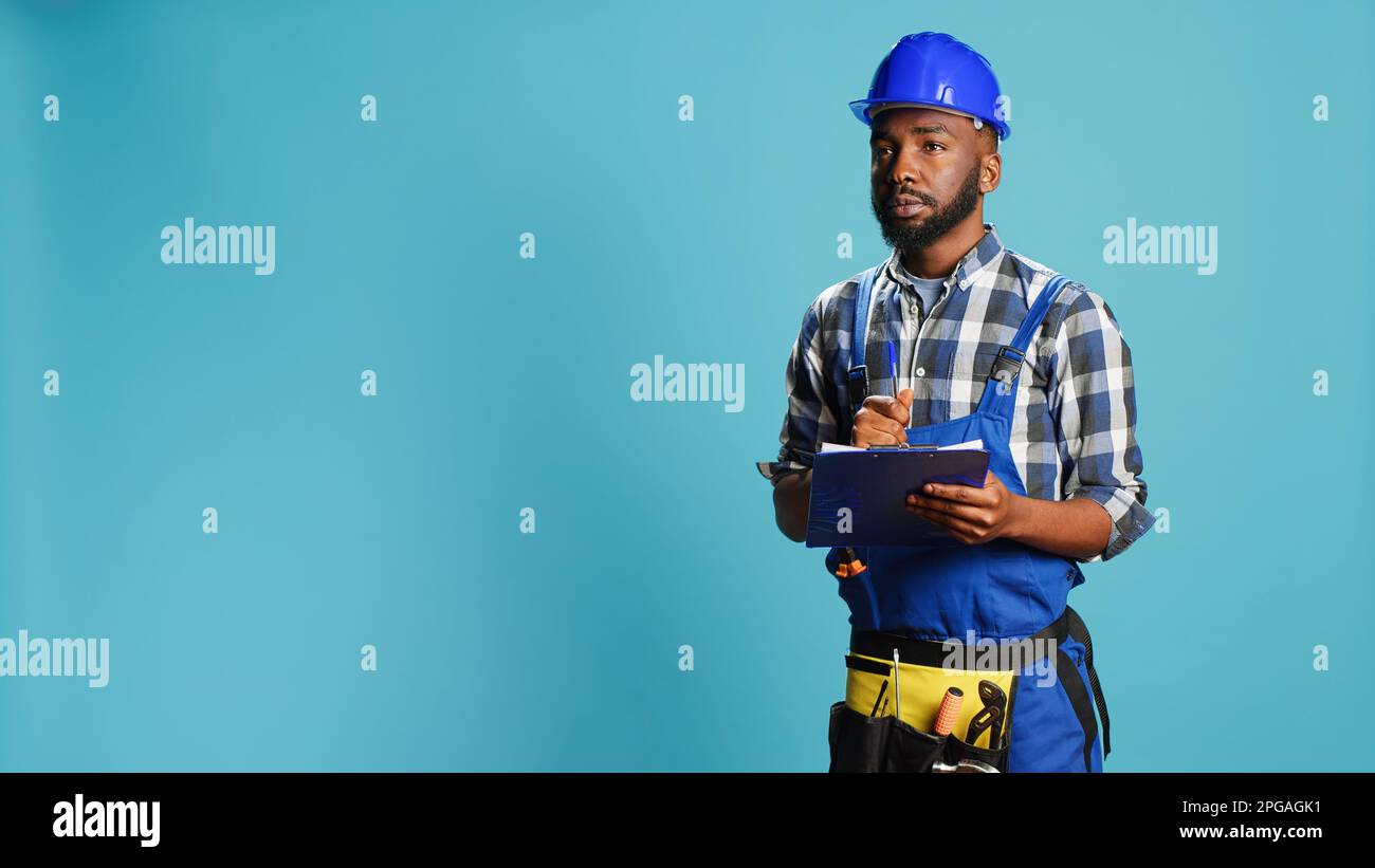 Young handyman making calculations on files, taking notes on papers ...