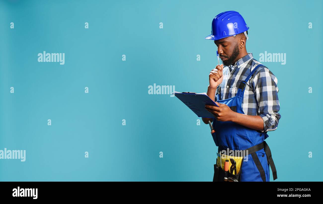 Confident builder making calculations on papers, taking notes on files ...