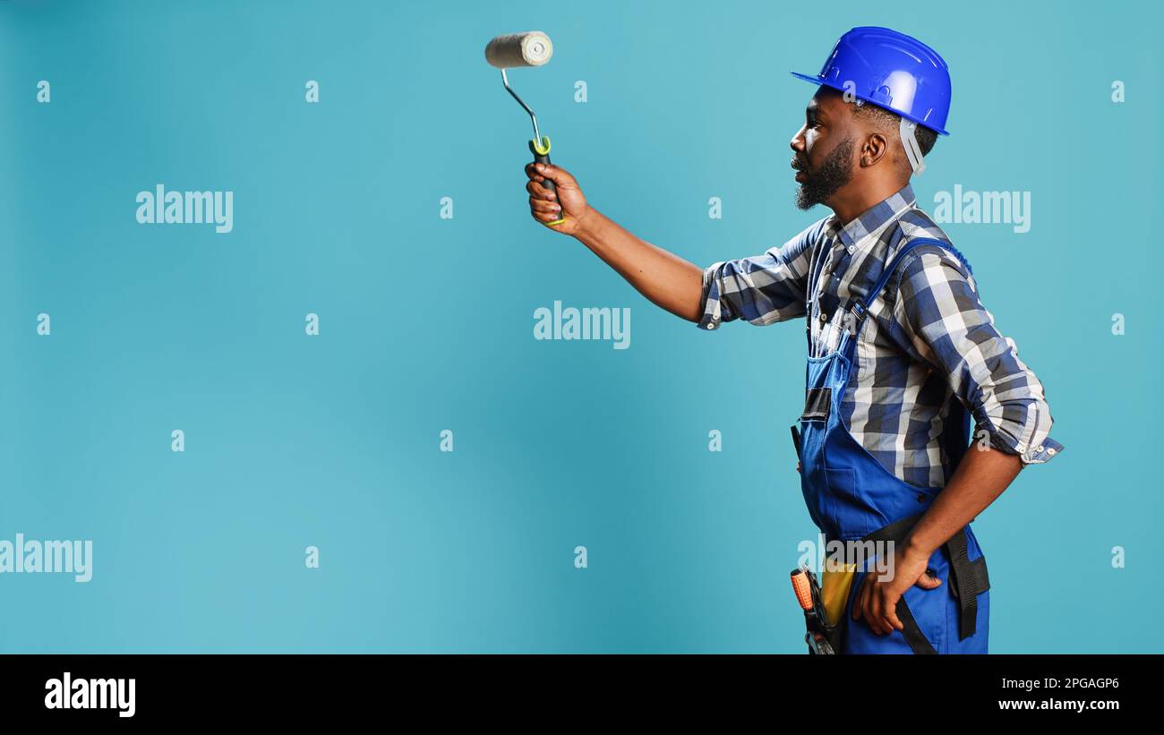 Industrial worker in uniform painting walls with roller, using ...