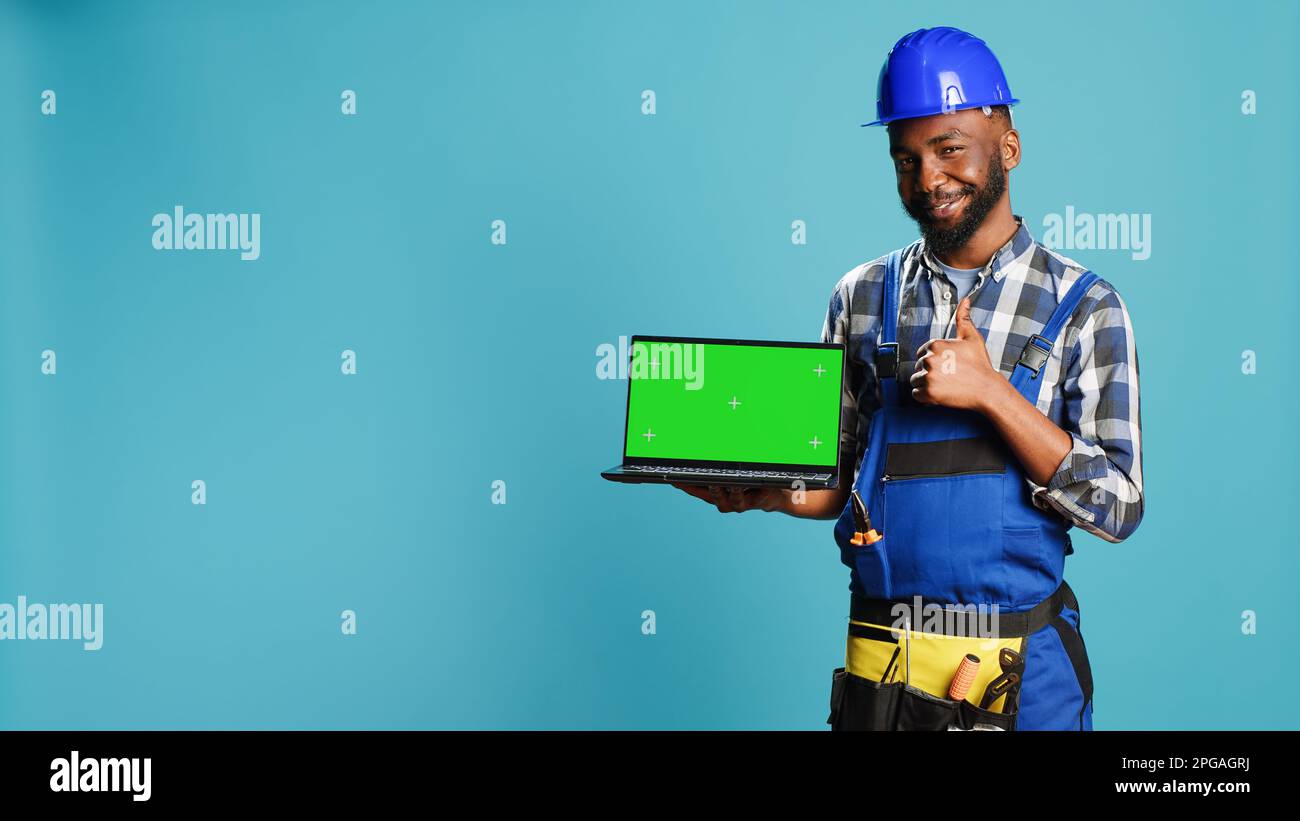 Happy mechanic pointing at laptop with greenscreen on camera ...
