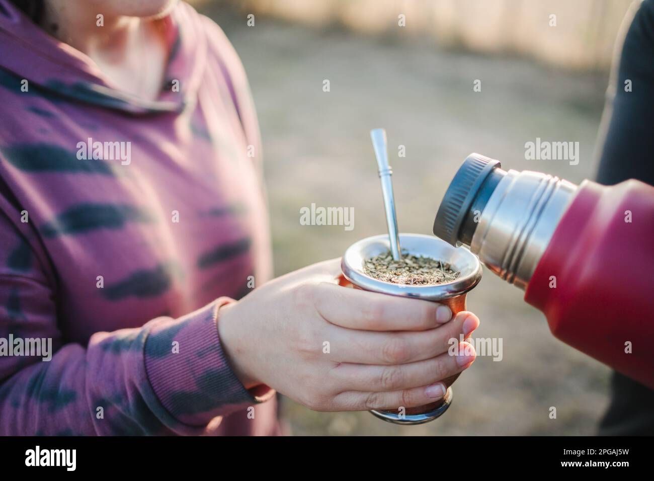 Two unrecognizable friends serving water with a thermo into yerba mate ...