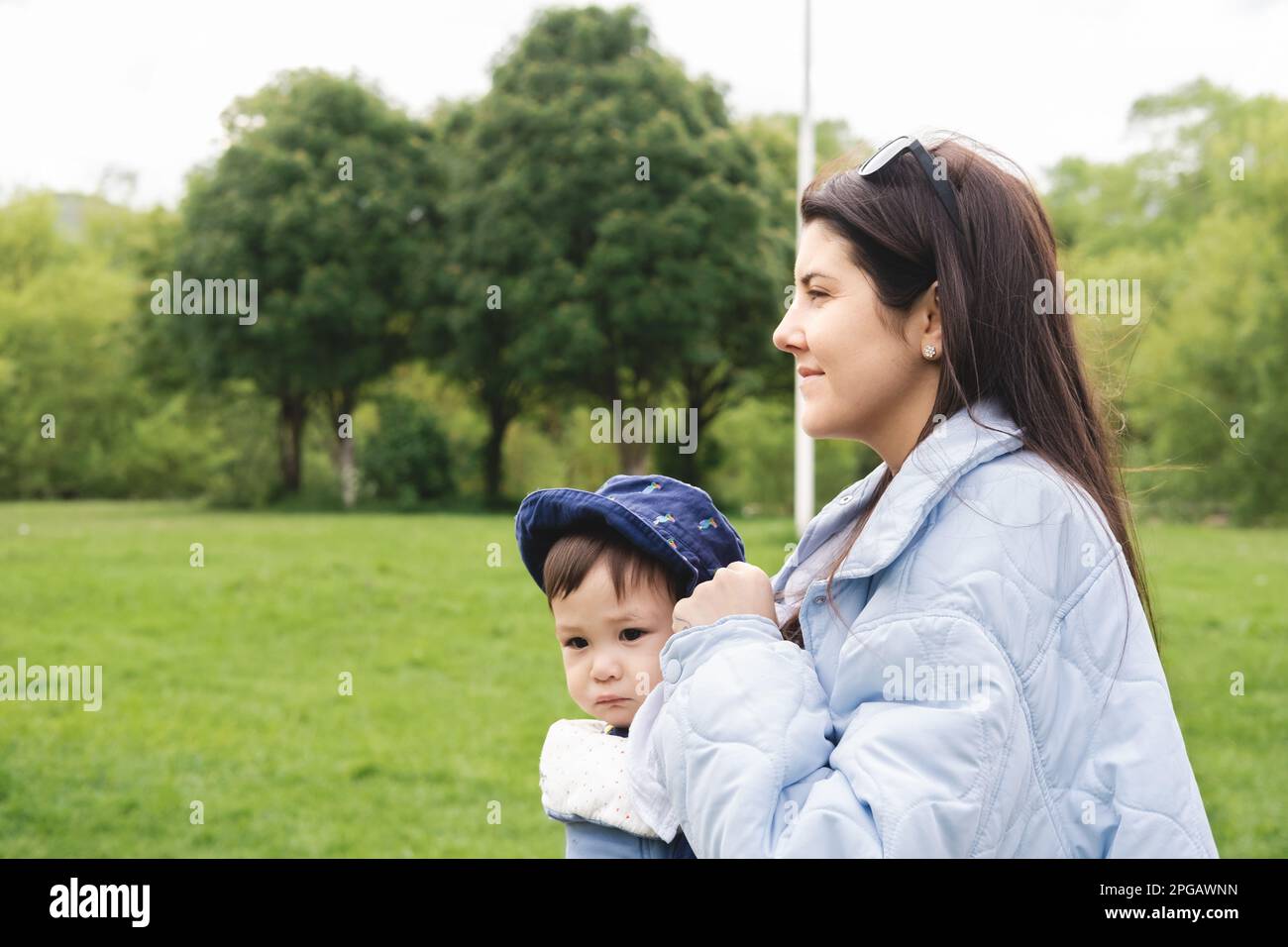 A mother carrying her male infant with a baby carrier while walking at ...