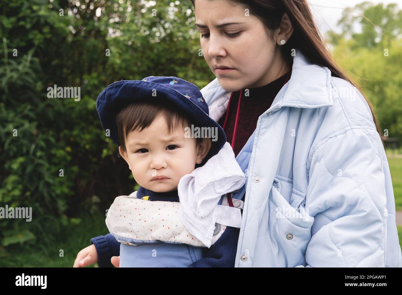 A male infant is looking at camera while being carried by his mother ...
