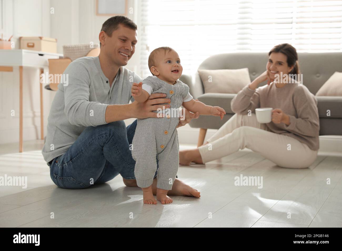 Father supporting his baby daughter while she learning to walk at home ...