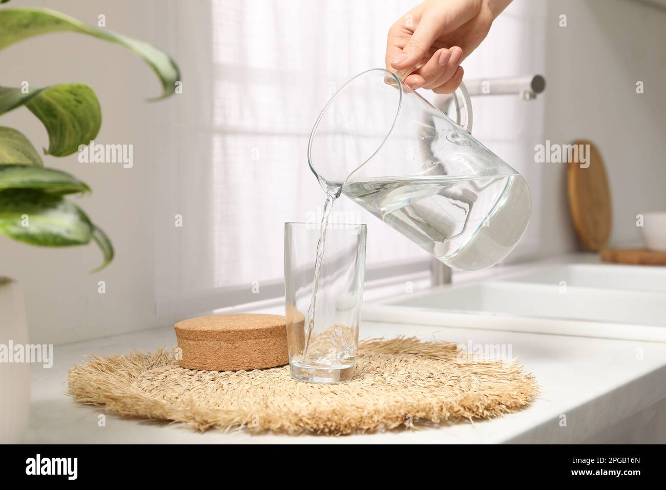 Woman pouring water into glass from jug on countertop in kitchen, closeup Stock Photo - Alamy