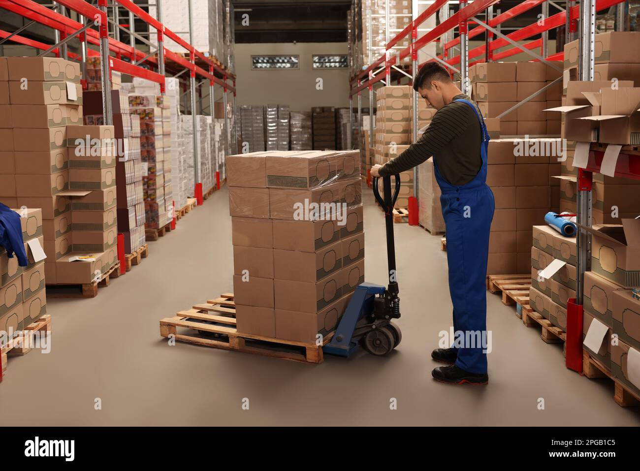 Worker pulling manual pallet truck with boxes wrapped in stretch film ...