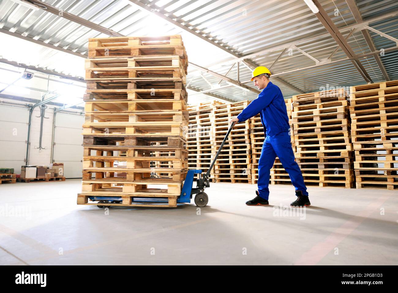 Worker moving wooden pallets with manual forklift in warehouse Stock ...