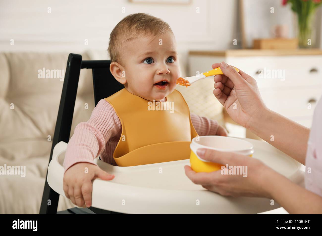 Mother feeding her little baby at home. Kid wearing silicone bib Stock ...