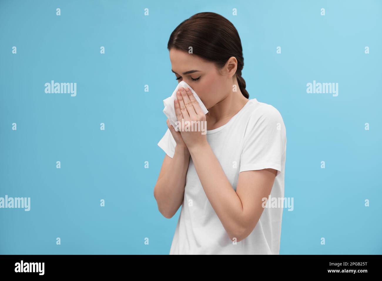 Woman blowing nose on light blue background. Cold symptoms Stock Photo ...
