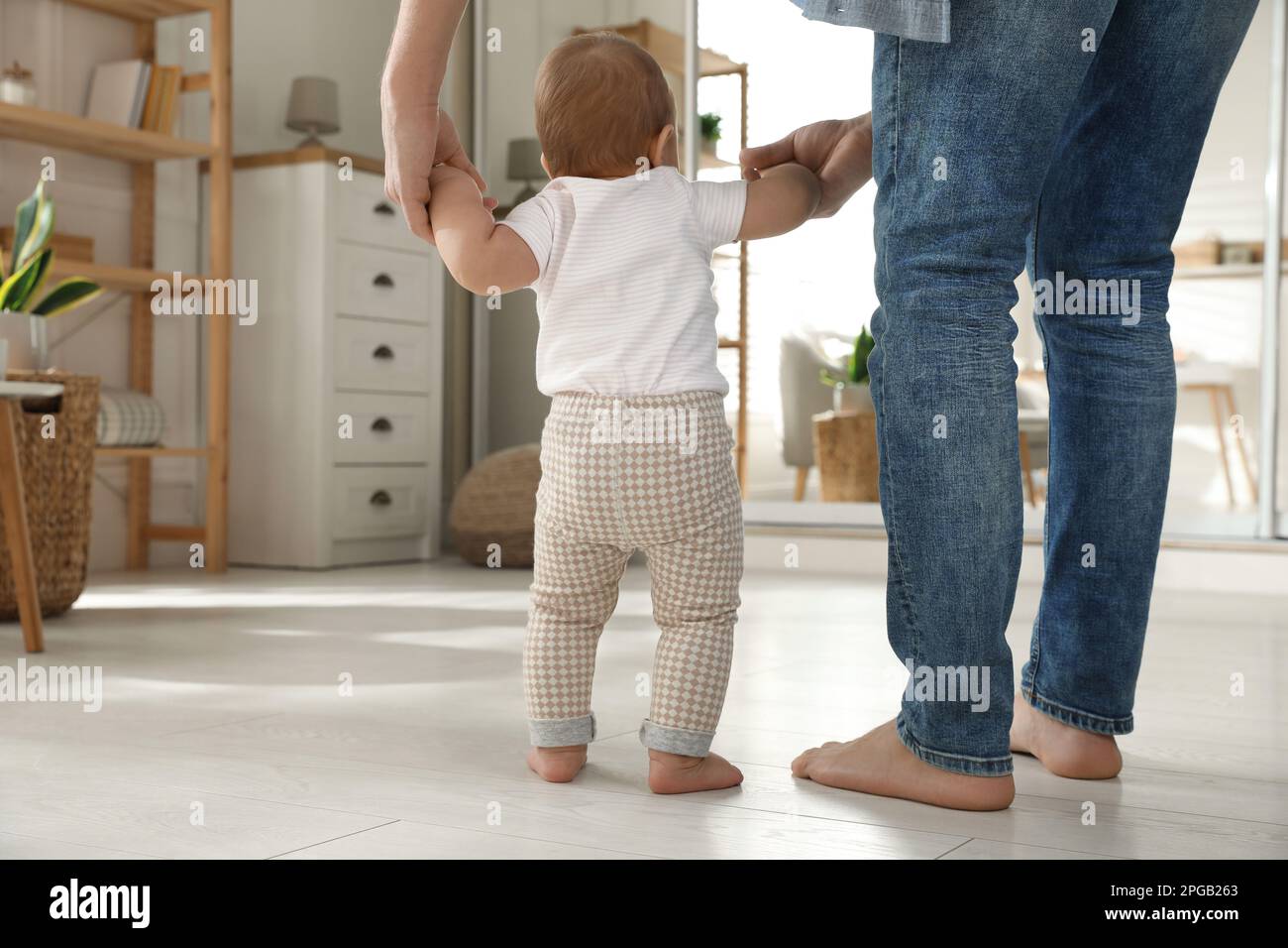 Father supporting his baby daughter while she learning to walk at home ...