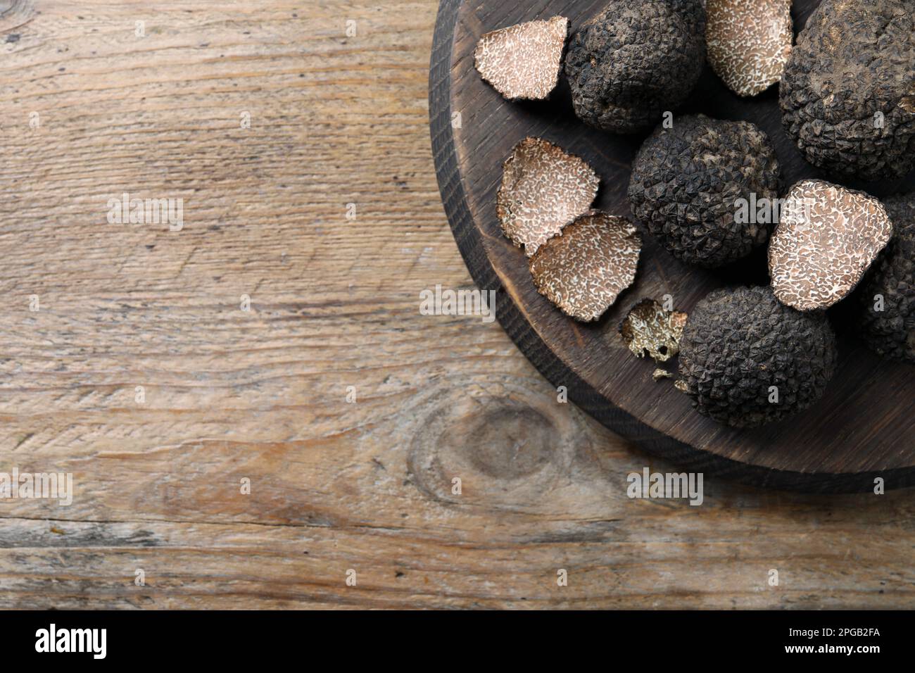Whole and cut black truffles with board on wooden table, top view ...