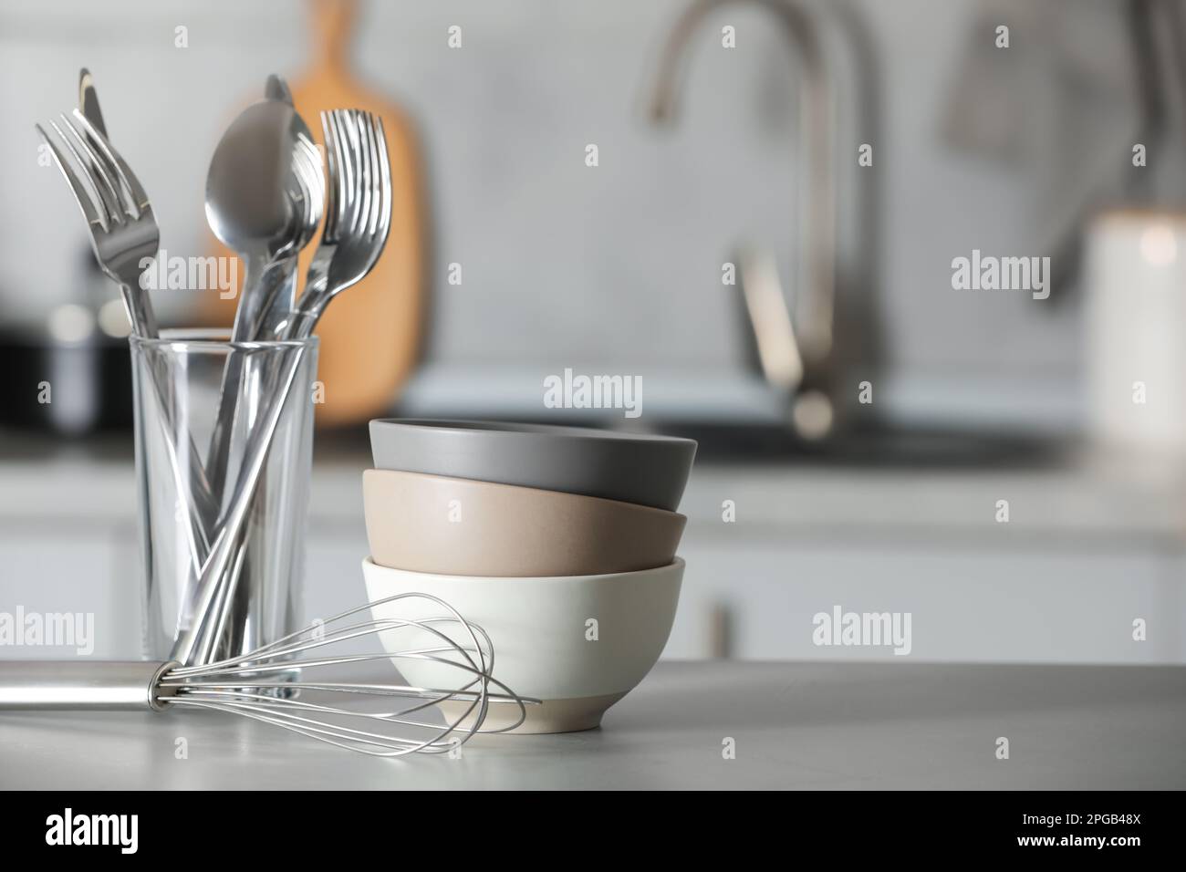 Set of eating utensils, balloon whisk and bowls on grey table in ...