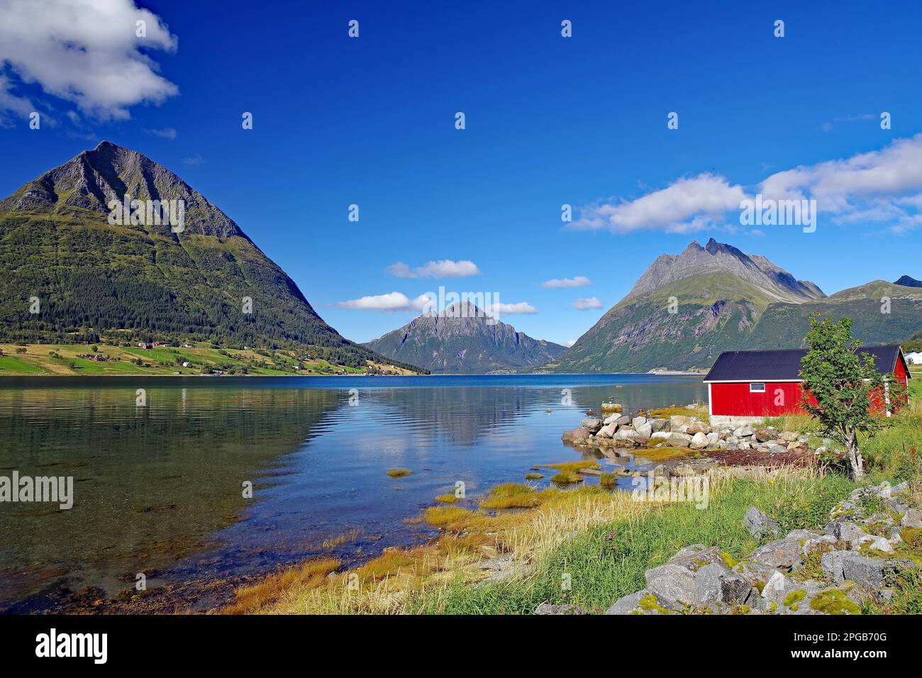 Red wooden house and high, rugged mountains by a fjord, shallow bay ...