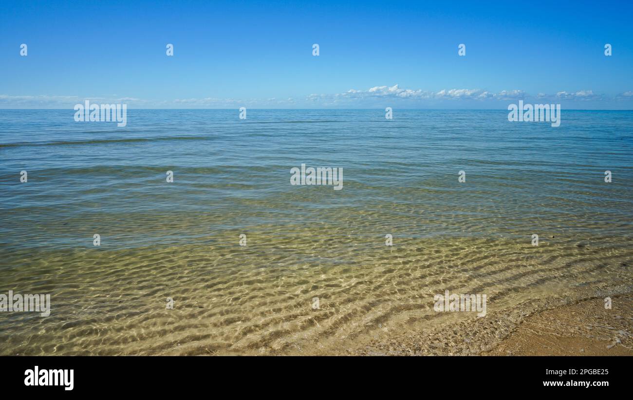 View from the shore, where gentle waves lap the sand, across crystal ...