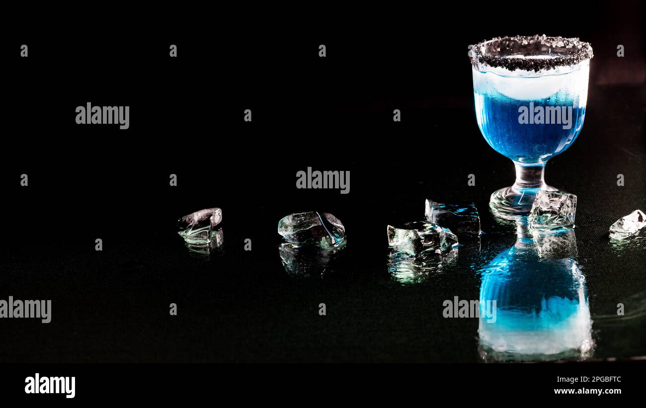 Blue margarita with black Hawaiian rim salt reflected on glass with ice ...