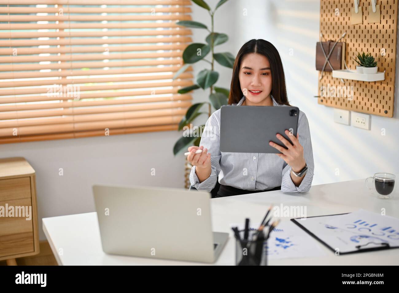 Focused young Asian female office worker using her digital tablet at ...