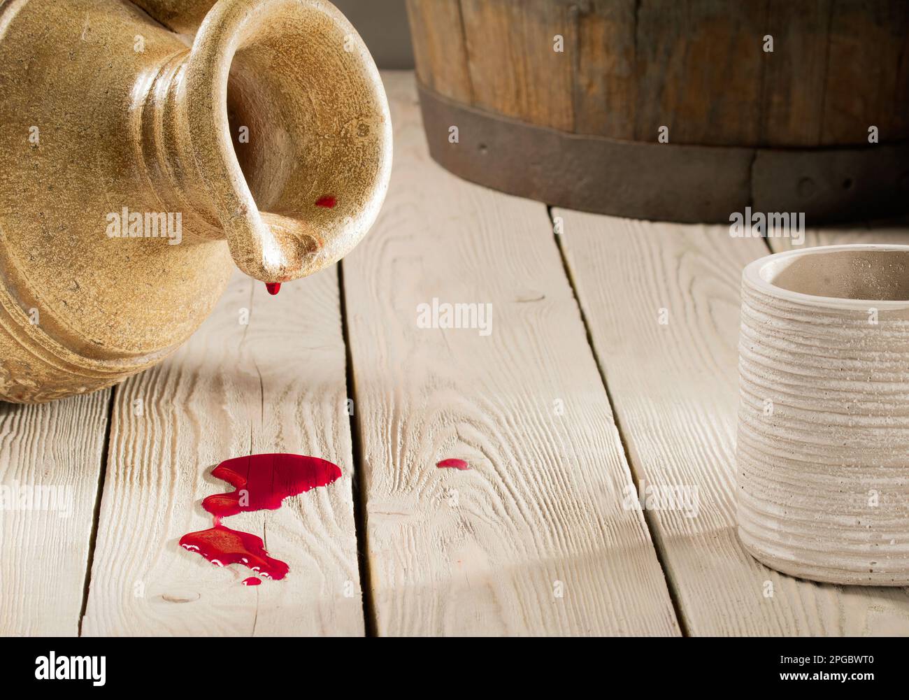 Clay wine jug, wine barrel and clay glass on a wooden table. A puddle ...