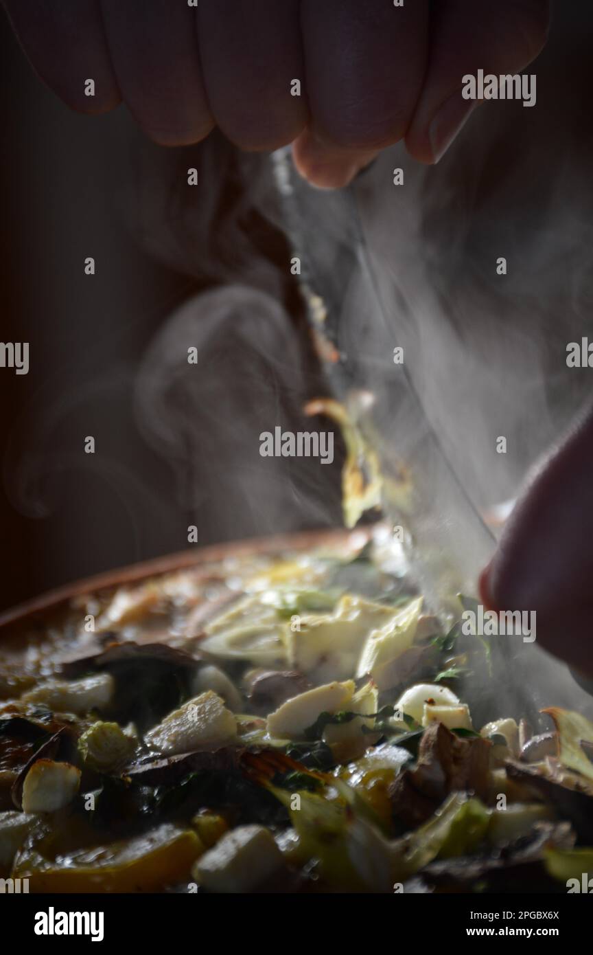 Swirling steam and two hands rocking a pizza-slicing blade to create ...