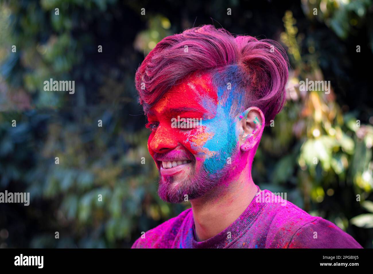 A young Indian man with his face smeared with multicolored powder ...