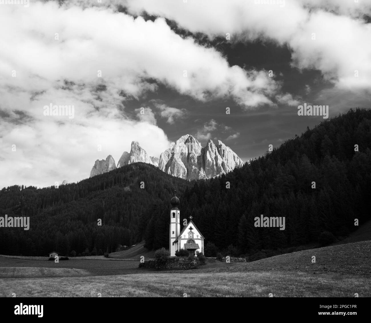 A grayscale shot of the church of St John set amid meadows & forested ...