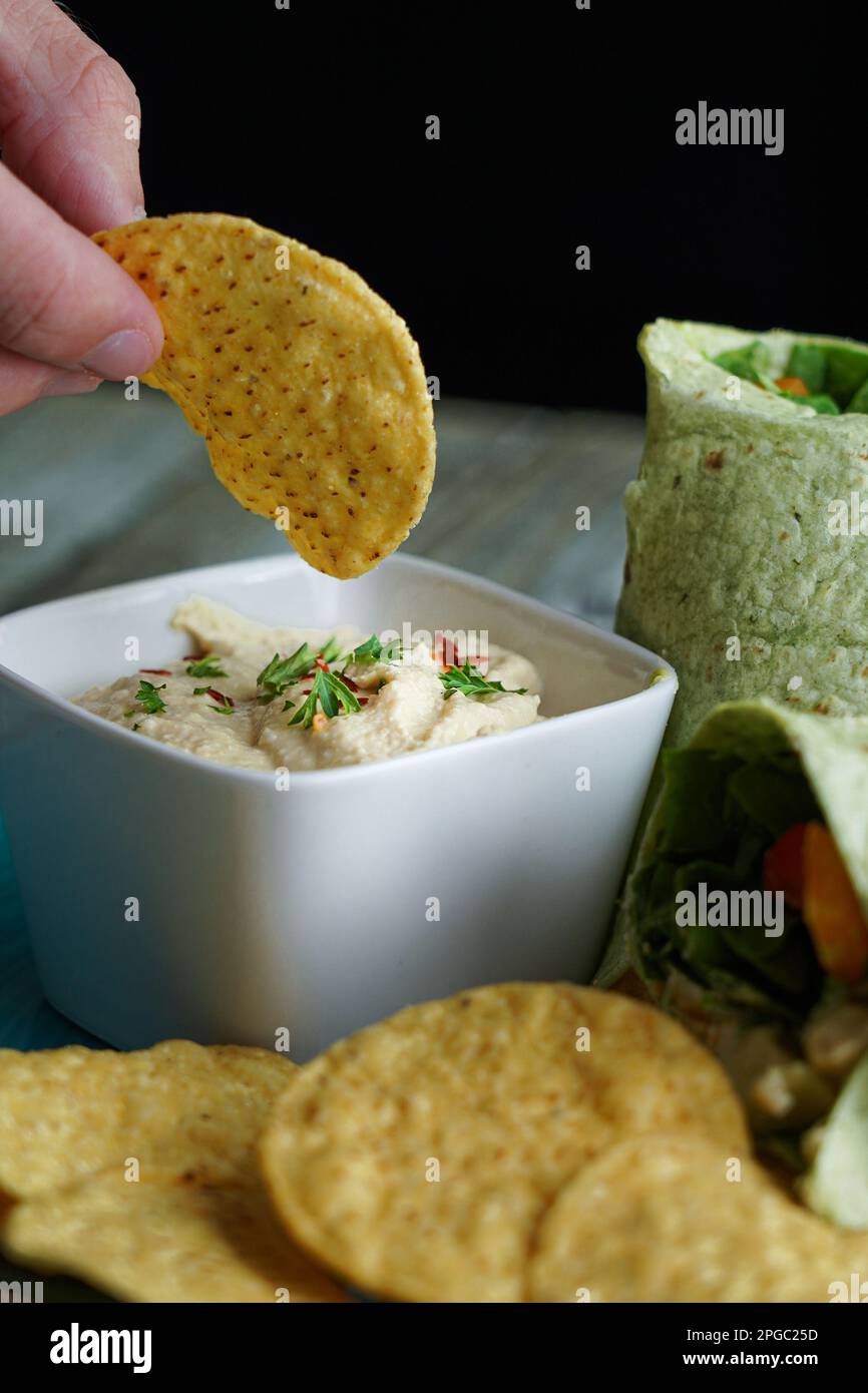 An individual enjoying a snack by dipping a chip into a bowl of dip ...