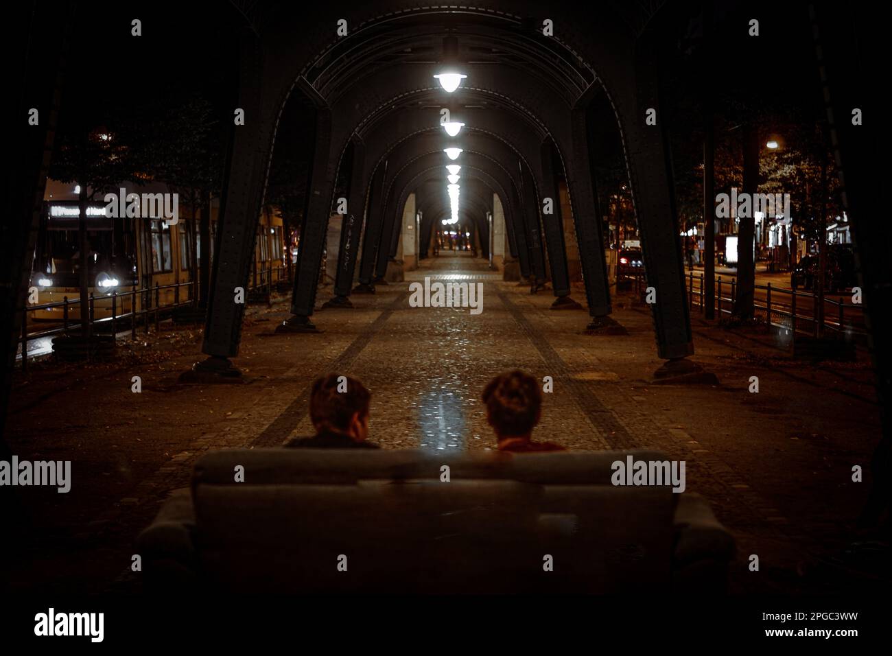 The two people sitting on a bench in an underground tunnel at night ...
