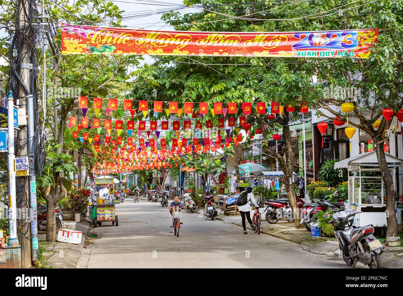 A little boy cycling down a strret decked with flags for Tet in Hoi An ...