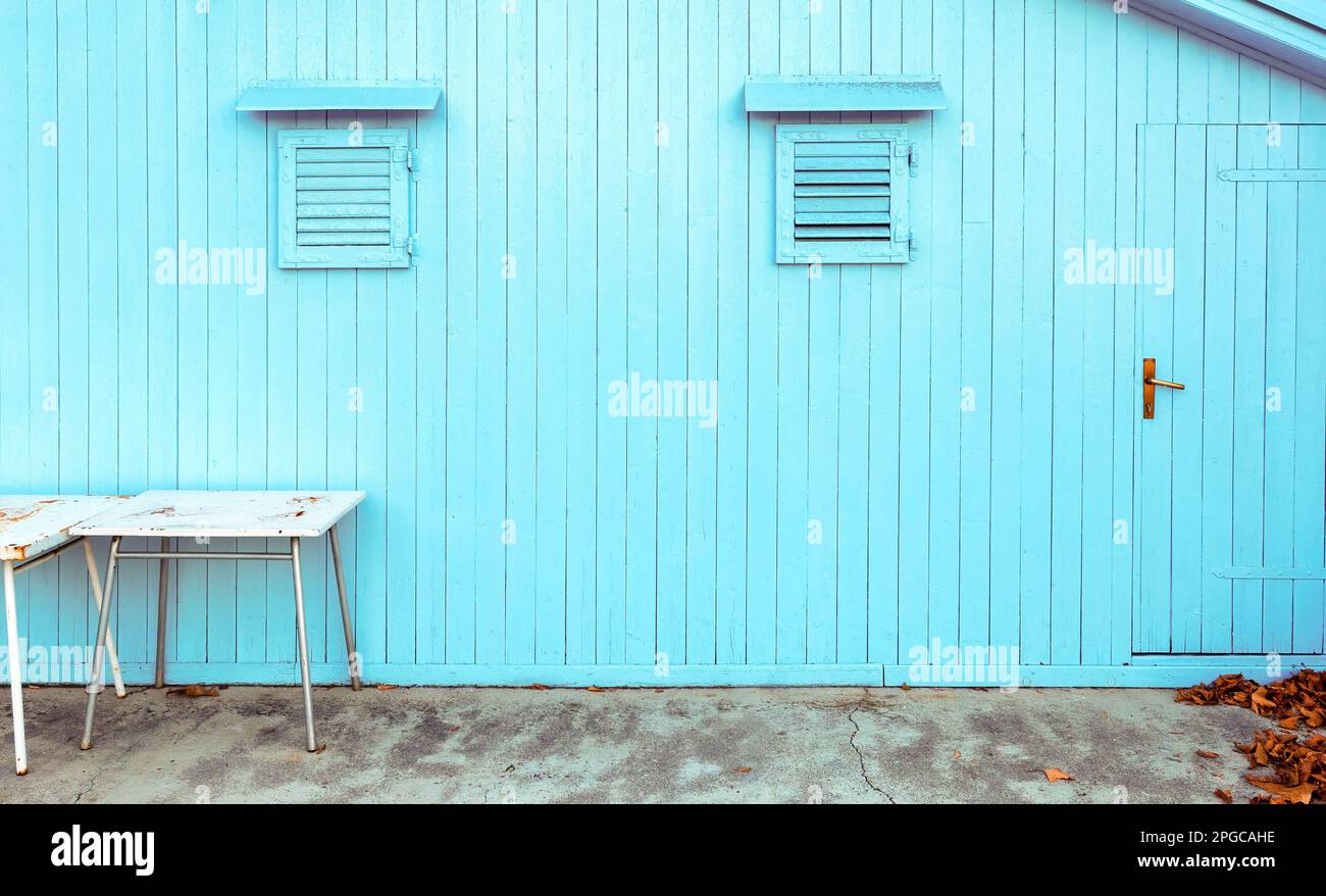 Blue wooden shed with small windows and two tables in front as ...