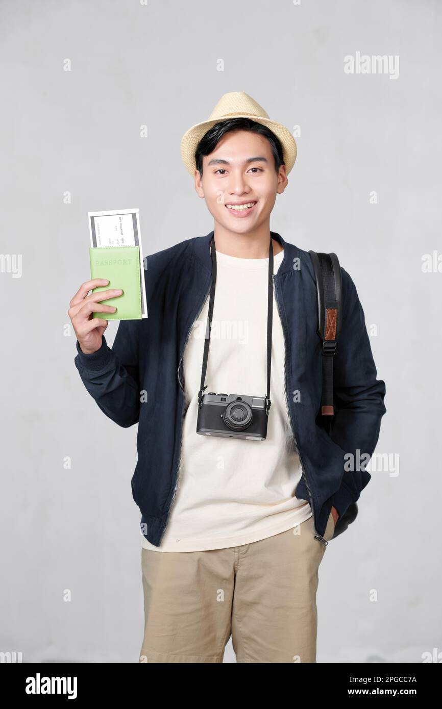 Portrait of happy young guy holding passport and boarding pass against ...