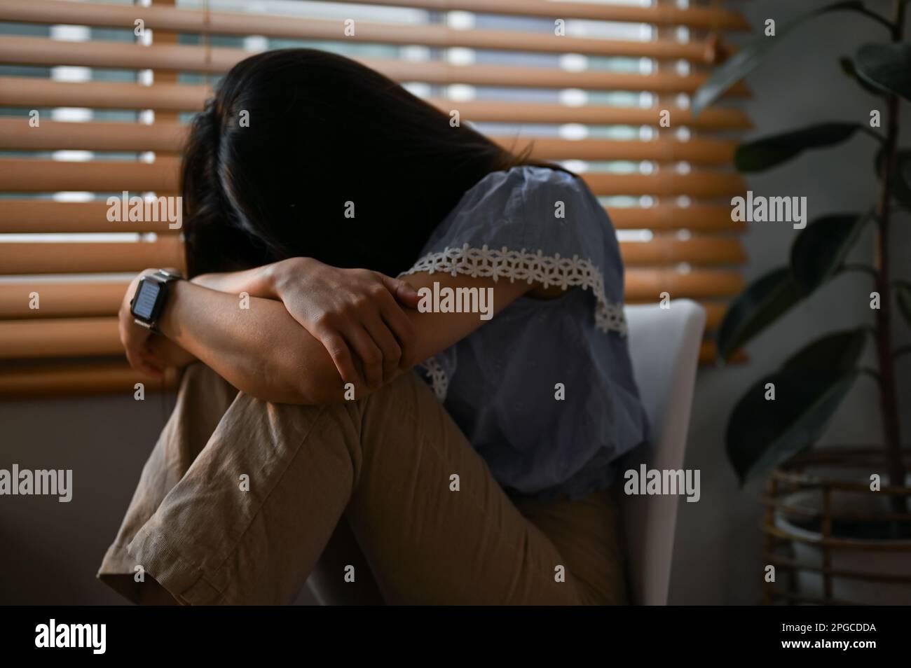 Sad and depressed young Asian woman sits near the window in dark living ...