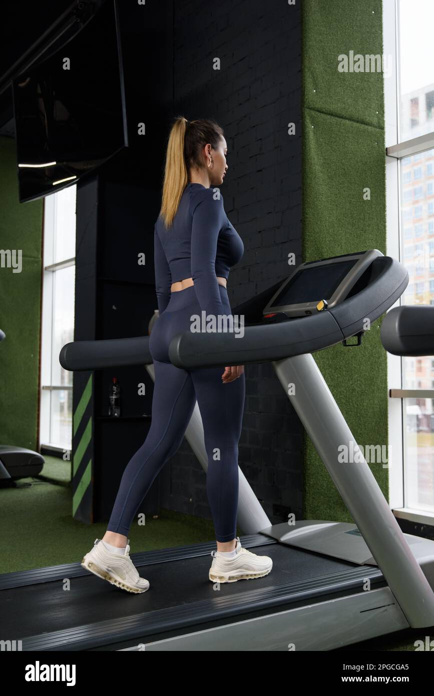 Beautiful muscular woman walking on a treadmill. wearing blue leggins ...
