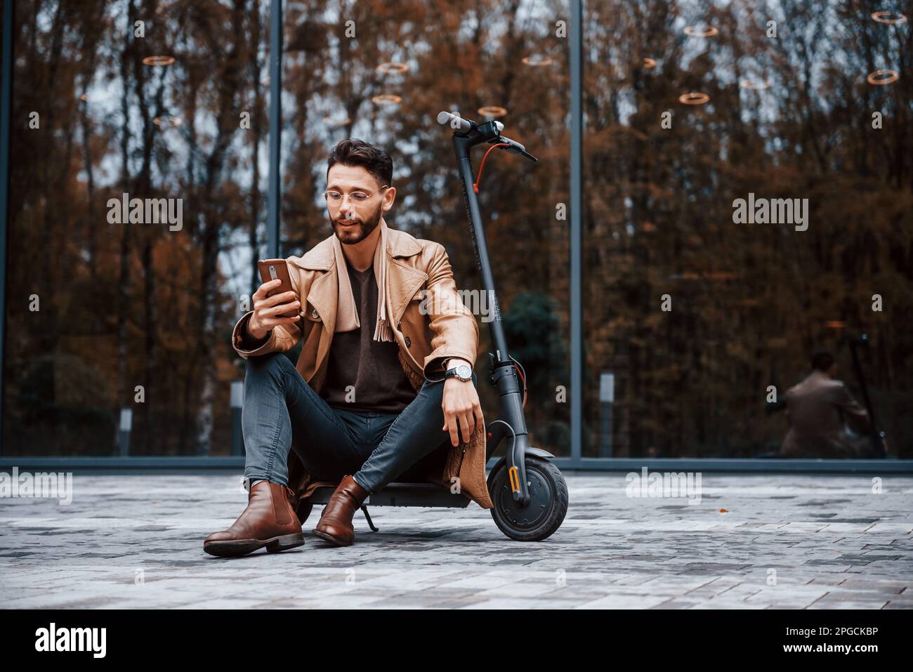Sits on electric scooter. Young male model in fashionable clothes is ...