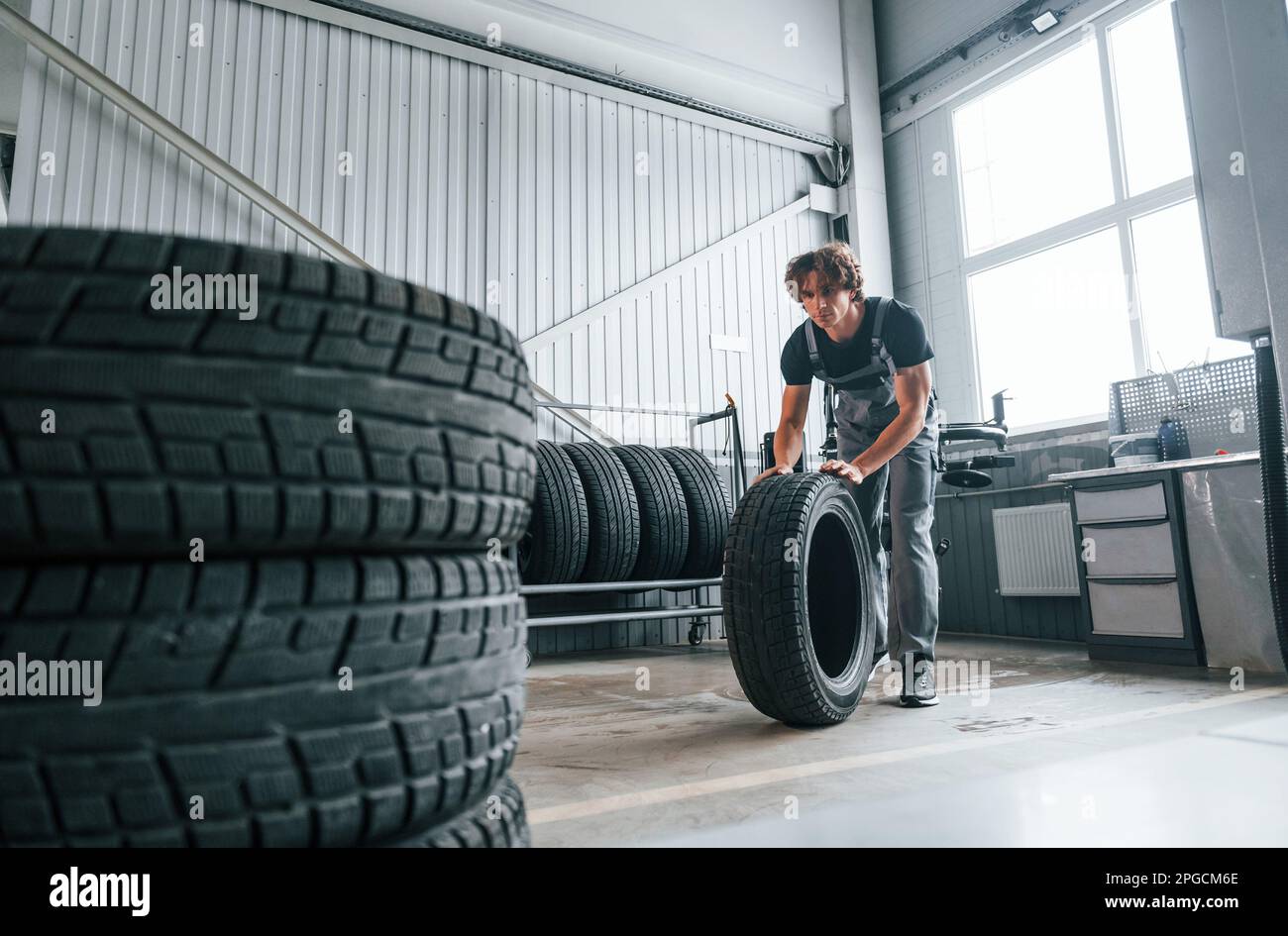 Rolls the tire. Adult man in grey colored uniform works in the ...