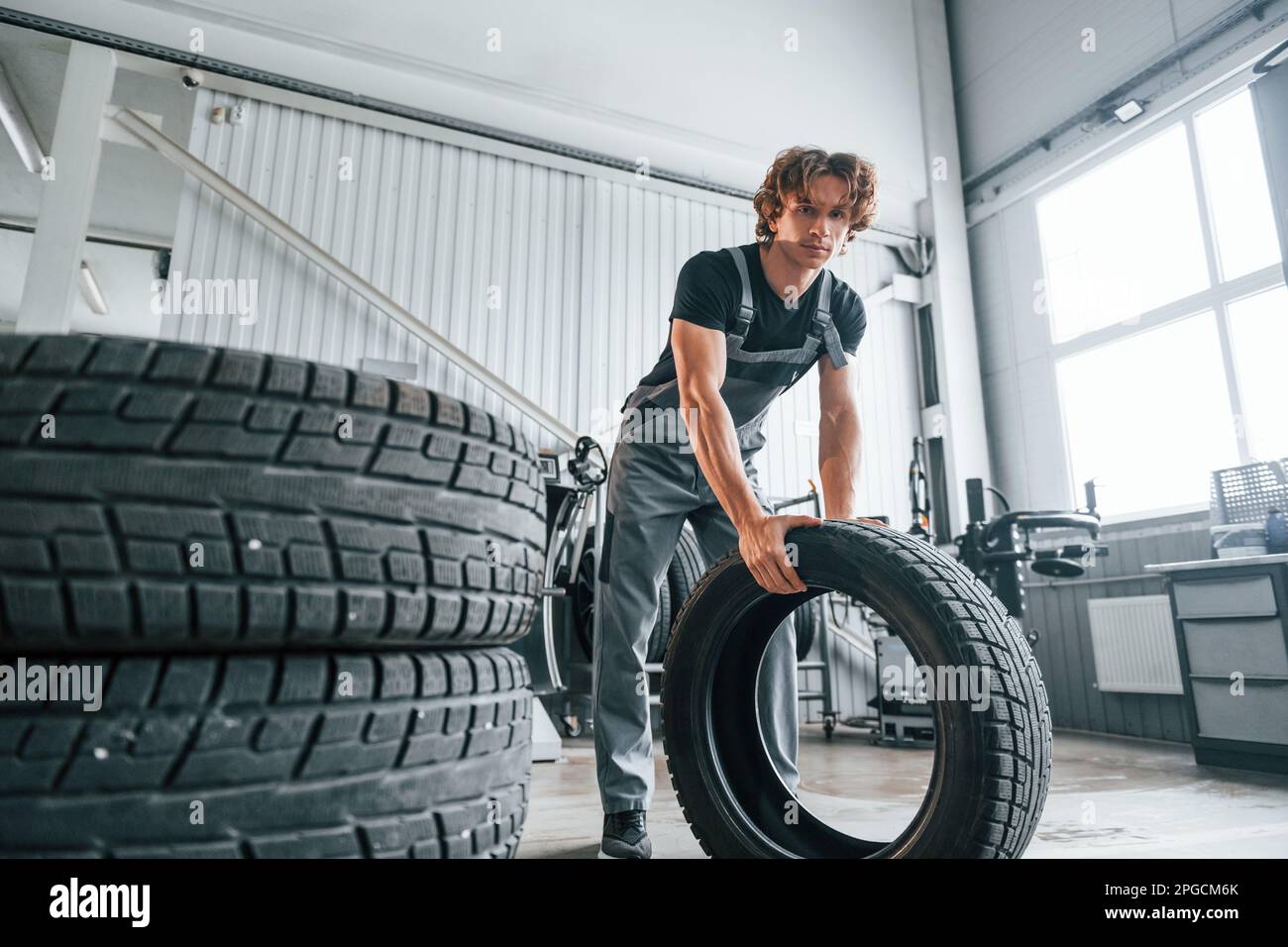 Rolls the tire. Adult man in grey colored uniform works in the ...