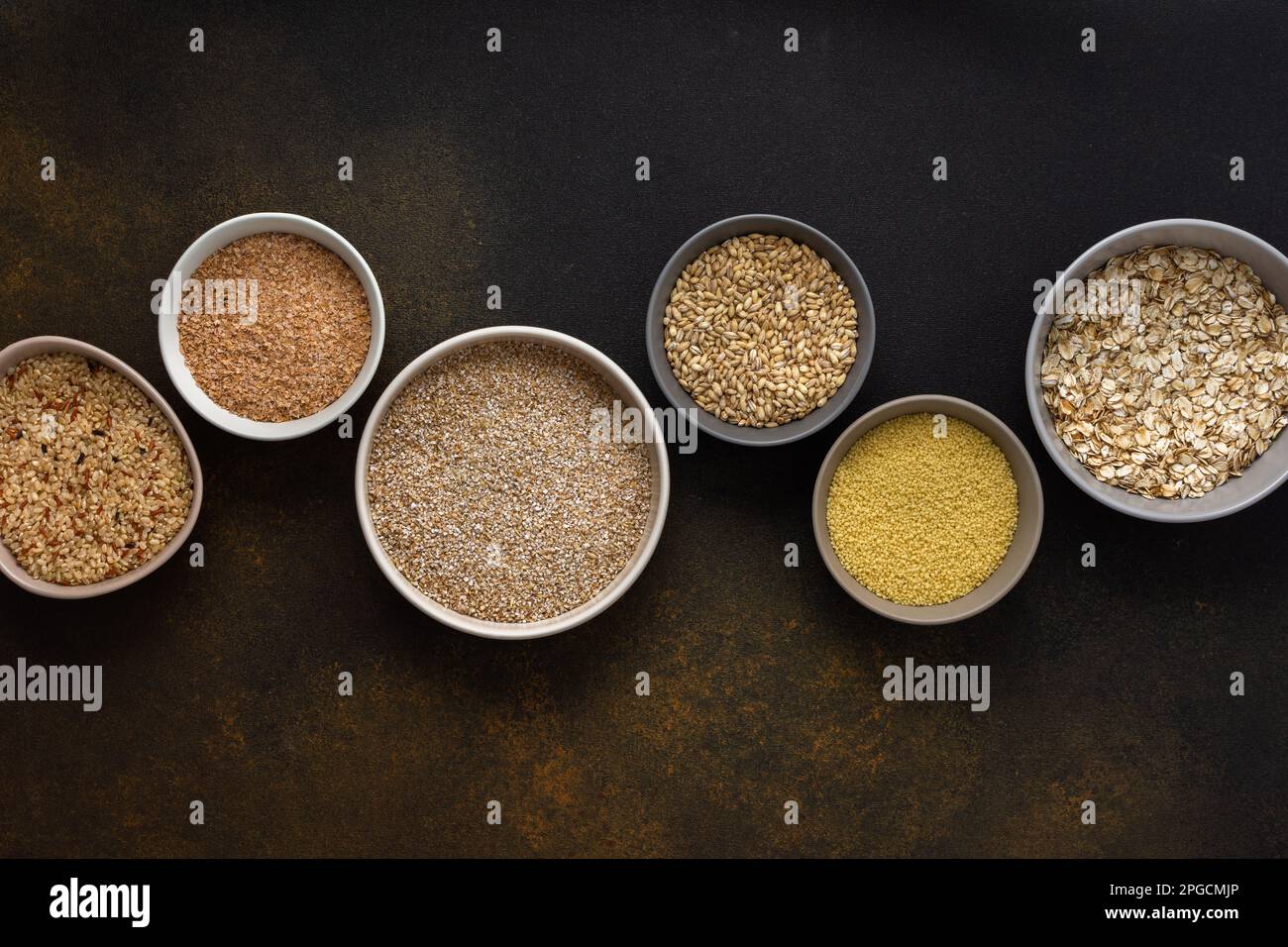 Various grain cereals in bowls, top view on a brown background with ...