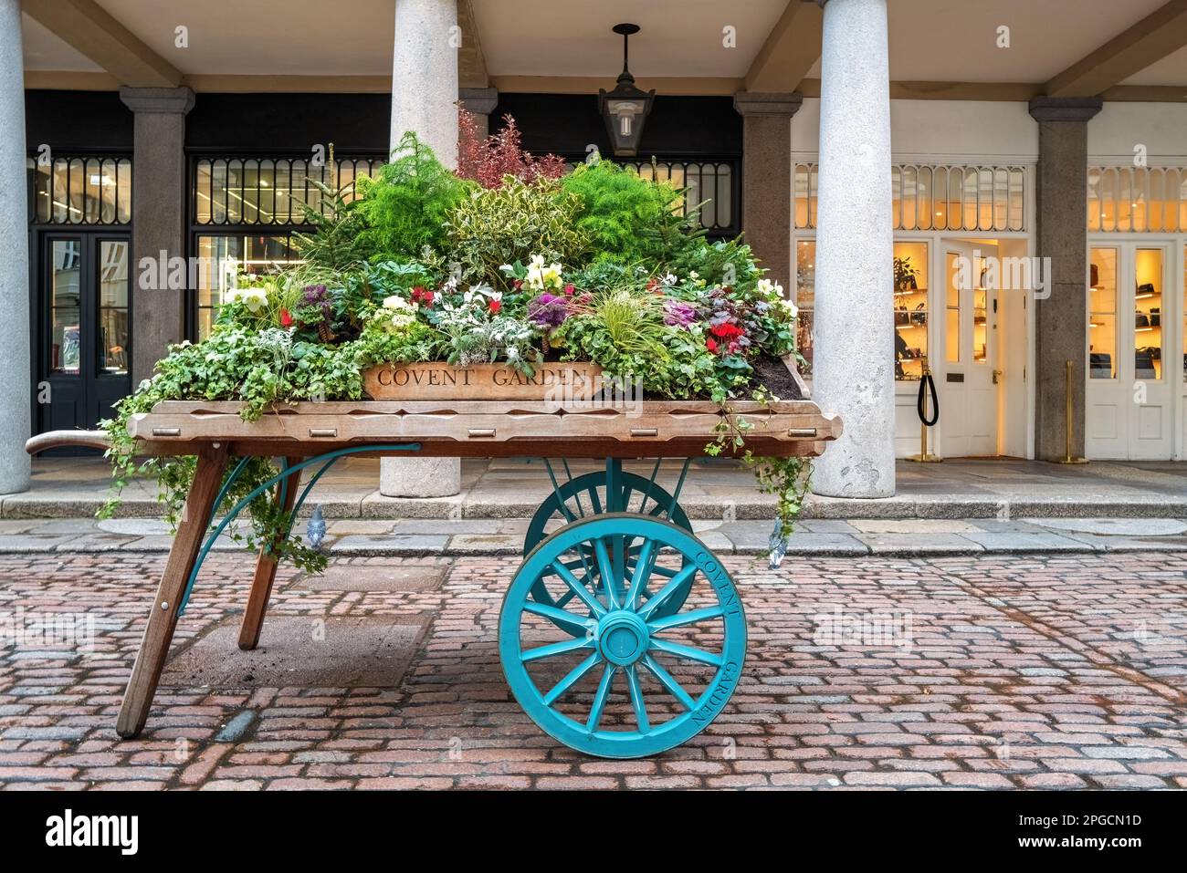 Old fashioned wooden barrow with boxes of flowers, outside the stores ...