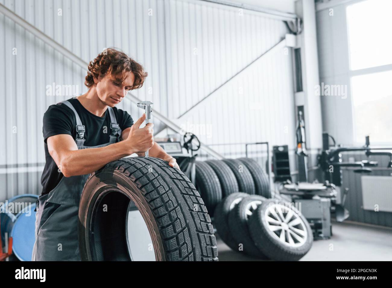 Works with tire. Adult man in grey colored uniform is in the automobile ...