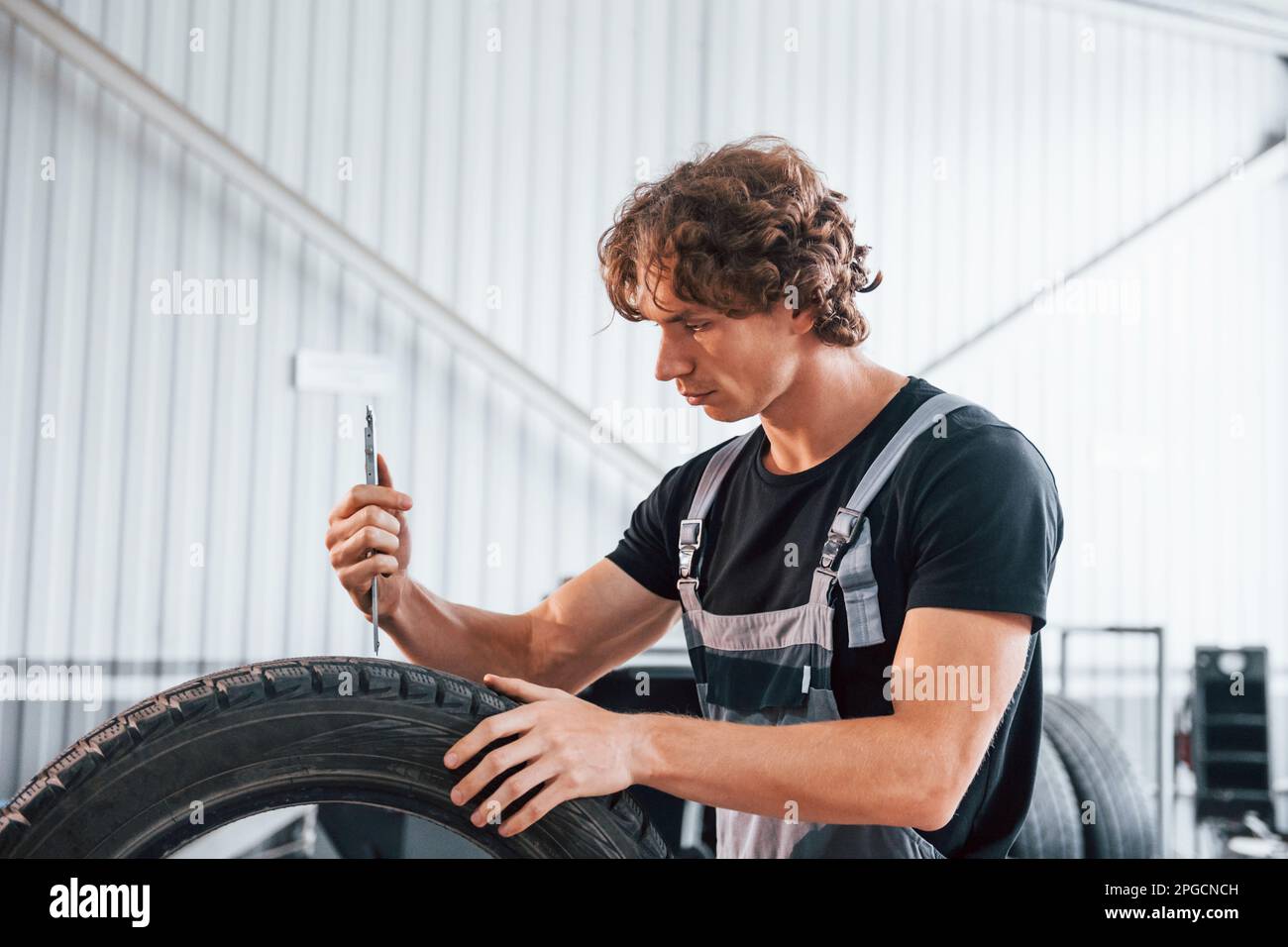 Works with tire. Adult man in grey colored uniform is in the automobile ...