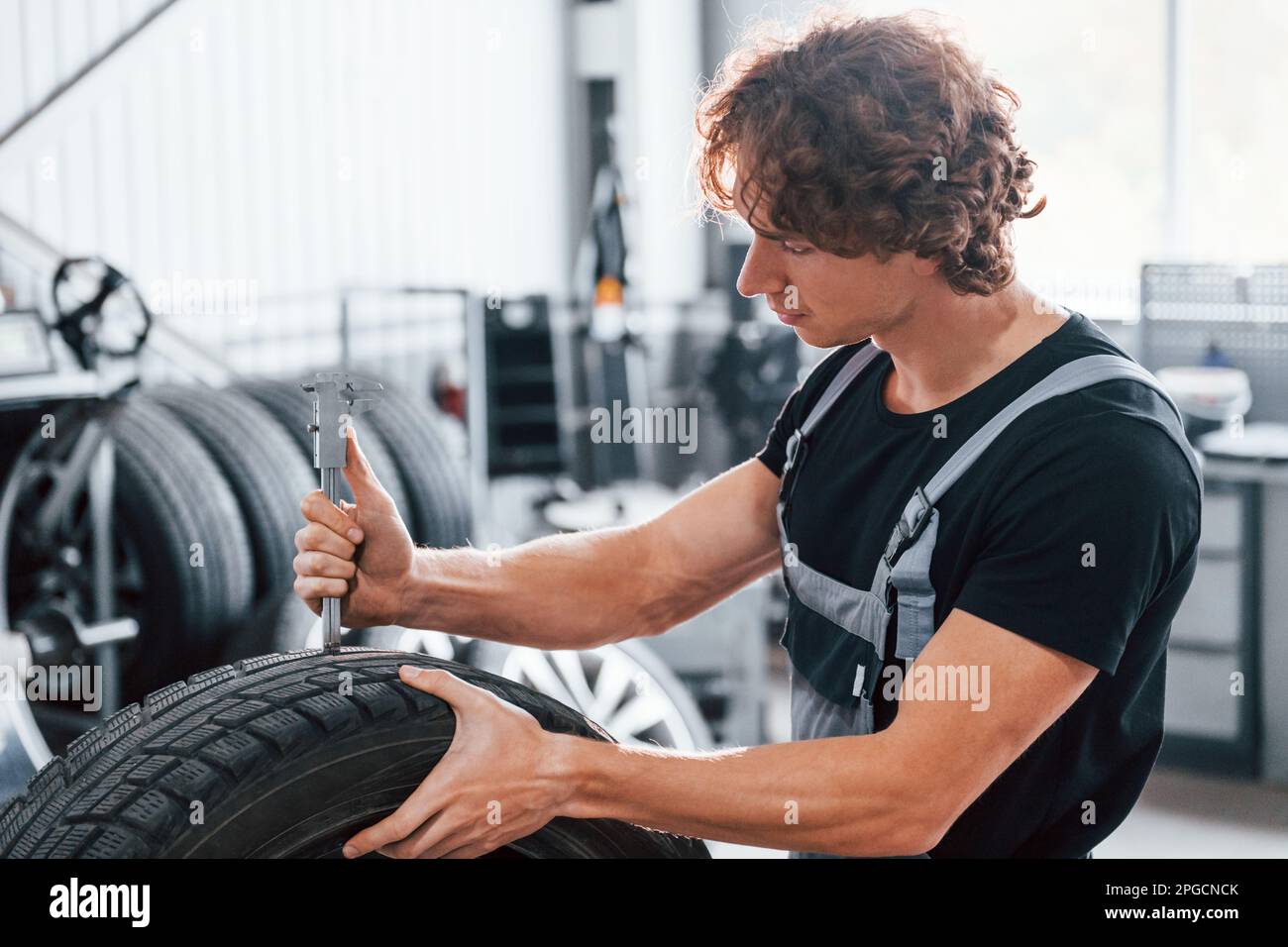 Works with tire. Adult man in grey colored uniform is in the automobile ...