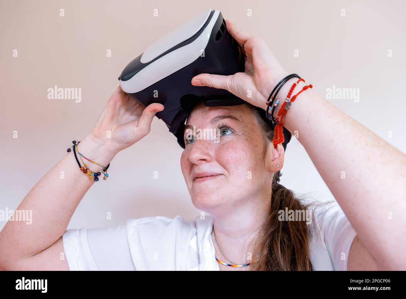 Smiling young female gamer removing VR goggles with hands from eyes and ...