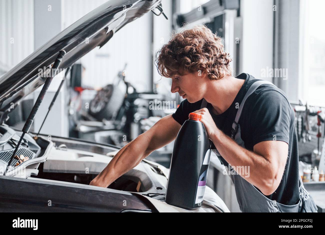 Changing oil. Adult man in grey colored uniform works in the automobile ...