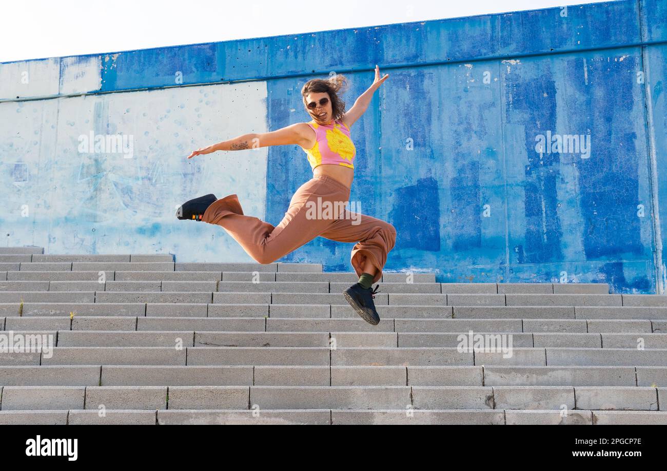 Active young female in casual clothes and sunglasses jumping above ...