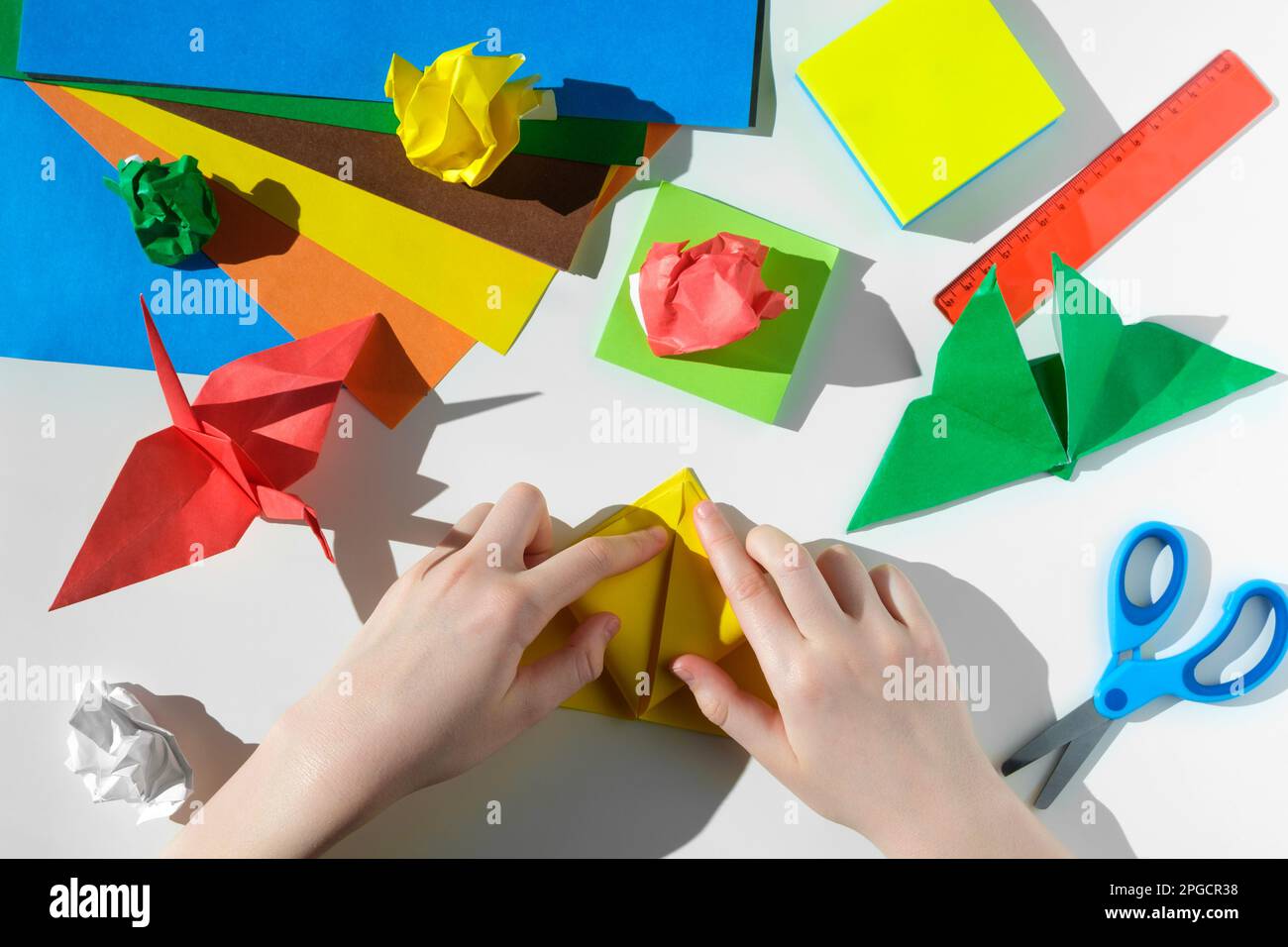 Paper crafts, scissors, colored paper sheets and scraps, on white table ...