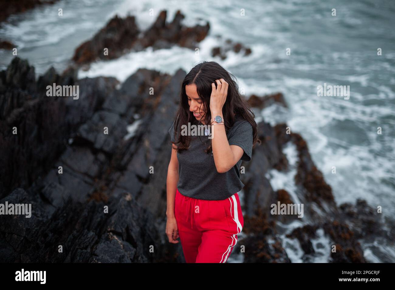 Positive young female standing on rocky cliff and looking away near ...
