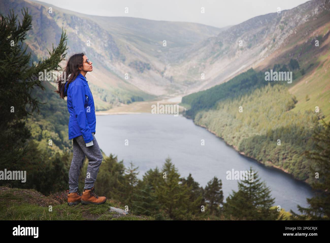 Side view of young female traveler standing on edge of hill in shade ...